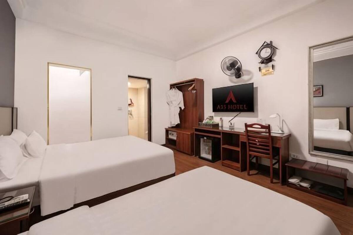 Quarto de hotel com duas camas, uma mesa com cadeira, televisão, guarda-roupa e espelho.