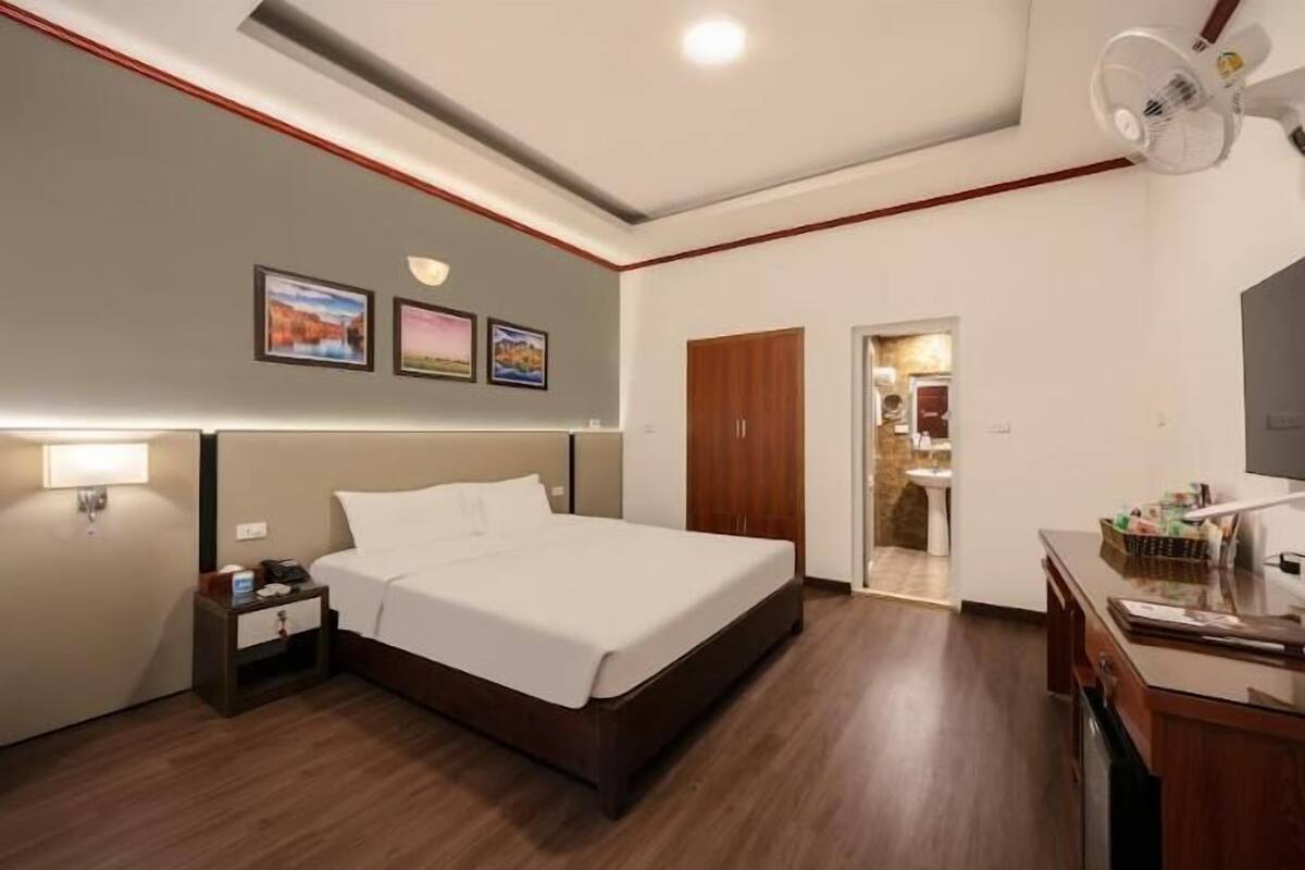 Quarto de hotel com cama, mesa de cabeceira, luminária e vista para o banheiro.