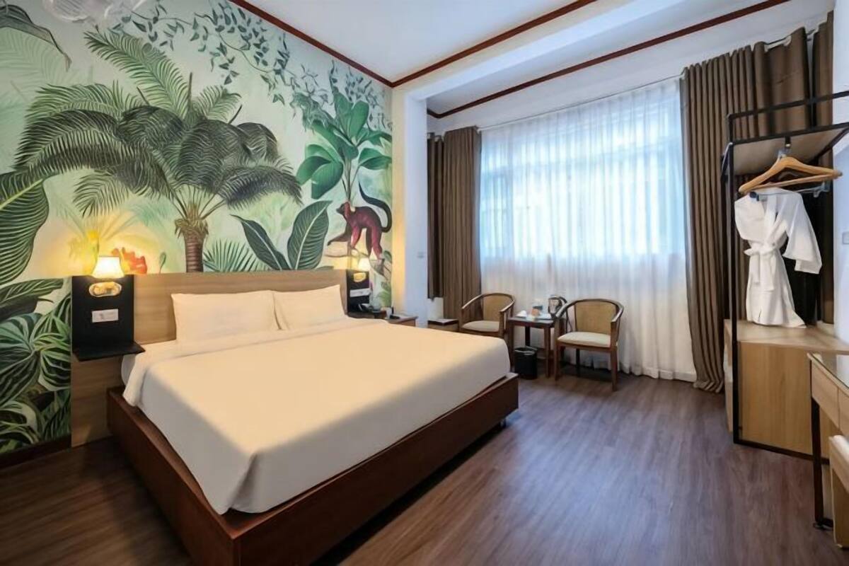 Quarto de hotel com uma cama grande, uma escrivaninha, uma cadeira, um guarda-roupa e um mural na parede.