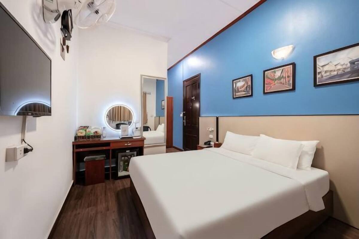 Quarto de hotel com cama, escrivaninha com espelho, cômoda e televisão fixada na parede.