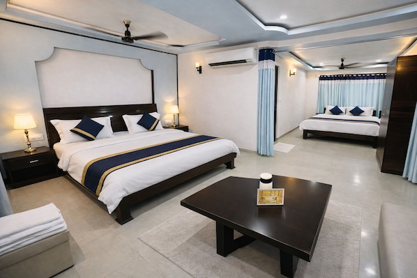 Quarto de hotel com uma cama grande, uma cama menor, uma mesinha de centro e uma mesa de cabeceira com abajur.