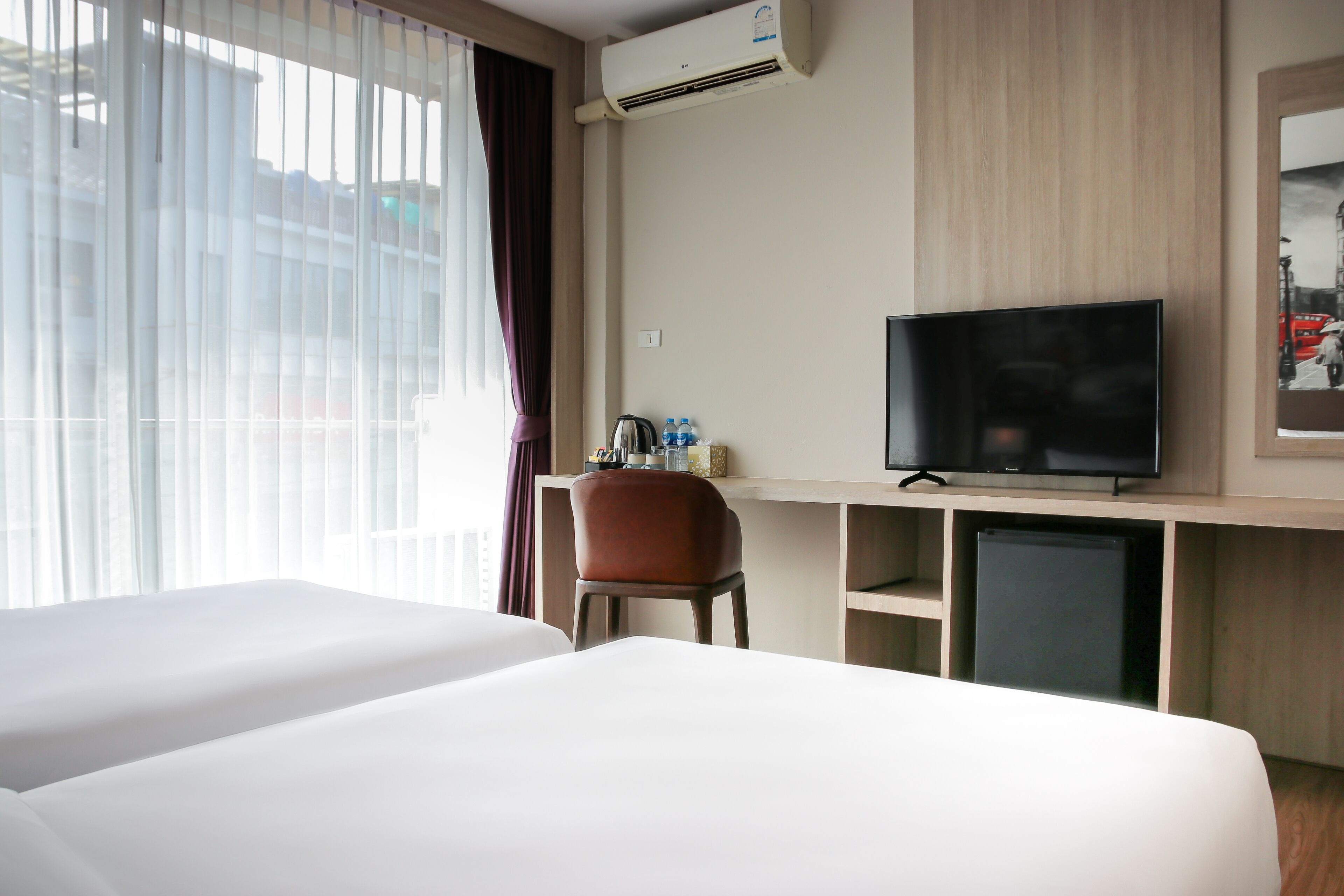 Quarto de hotel com duas camas, uma mesa de trabalho, televisão, uma cadeira e um pequeno frigorífico.