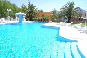 Piscina com um gazebo de madeira, espreguiçadeiras e palmeiras.