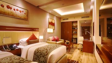 Quarto de hotel com cama, escrivaninha, cadeira, sofá, luminária, quadro e televisão.