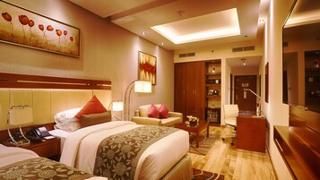 Quarto de hotel com cama, escrivaninha, cadeira, sofá, luminária, quadro e televisão.