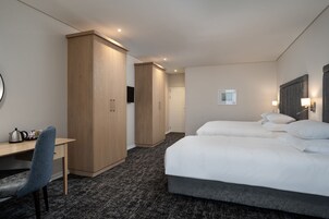 Quarto de hotel com uma mesa, duas camas, um guarda-roupa e uma janela pequena.