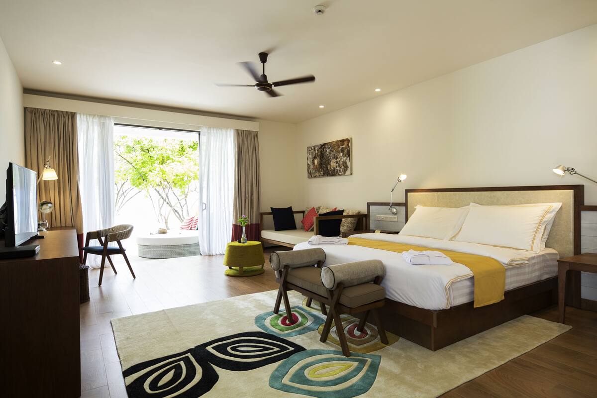 Quarto de hotel moderno com uma cama grande, uma escrivaninha, uma cadeira e vista para o exterior.