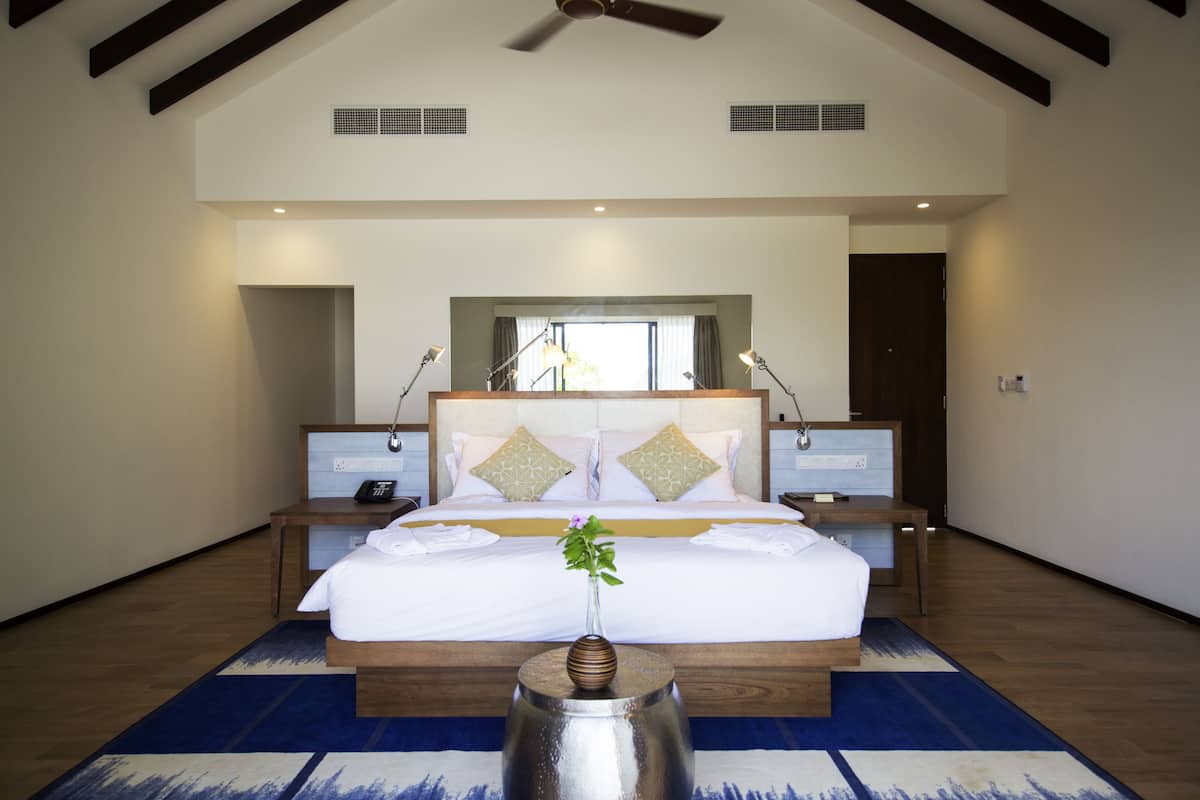 Quarto de hotel moderno com uma cama grande, mesas de cabeceira, ventoinha no teto e vista para o exterior.