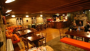 Um restaurante acolhedor com mesas e bancos de madeira, paredes de pedra e um espaço de bar.