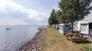 Um parque de campismo à beira do lago, com mesas de piquenique, veículos recreativos e margem rochosa.