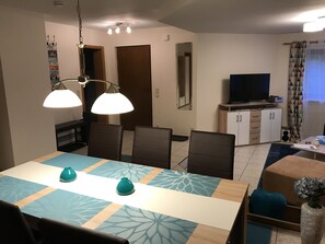 Uma área de refeições com uma mesa, cadeiras e uma televisão ao fundo.