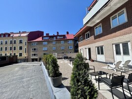 Um terraço no telhado com área de estar externa, plantas em vasos e vista para edifícios altos com fachadas vermelhas e bege.