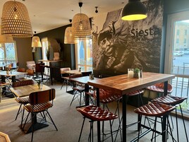 Interior de restaurante com mesas e cadeiras de madeira, luminárias pendentes e um grande mural na parede.