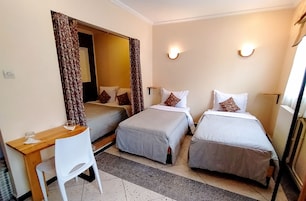 Quarto de hotel com duas camas de solteiro, uma escrivaninha de madeira, uma cadeira e um espelho.