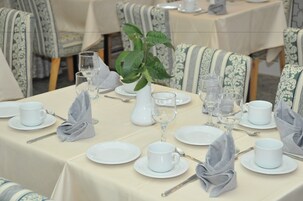 Mesa de jantar posta com pratos brancos, xícaras e talheres, rodeada por cadeiras listradas.