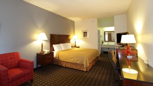 Quarto de hotel com uma cama, duas luminárias de cabeceira, uma poltrona vermelha, uma escrivaninha com luminária e uma televisão.