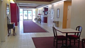 Um saguão de hotel com balcão de recepção, área de espera com cadeiras e espaço de refeições com mesa e cadeiras.