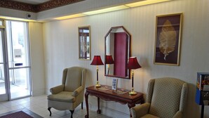 Um saguão de hotel com dois poltronas, uma mesa com luminárias, um espelho e uma obra de arte com folha emoldurada.