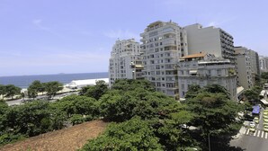 Um edifício alto com várias varandas, vista para o mar e vegetação ao redor.