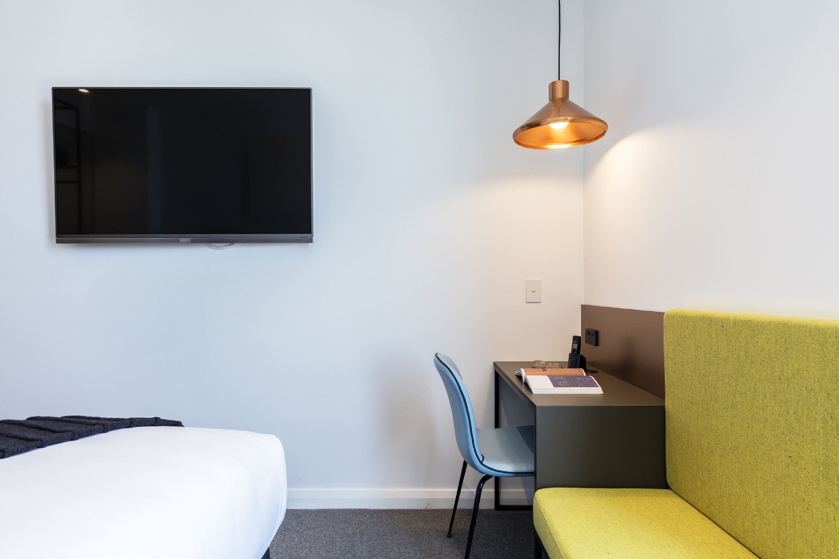 Quarto de hotel moderno com cama, escrivaninha, cadeira e televisão na parede.