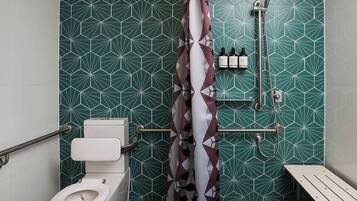 Um banheiro com padrão de azulejos geométricos, vaso sanitário branco, chuveiro com chuveiro manual e um banco.