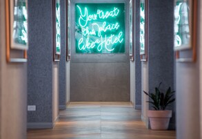 Um corredor com um letreiro de neon que diz: "Trate este lugar como um hotel".