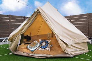 Uma tenda com área para dormir, um candeeiro e almofadas decorativas.