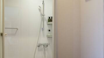 Um chuveiro sem barreiras, com porta de vidro, uma prateleira branca com artigos de higiene e um porta-toalhas na parede.