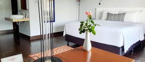 Quarto de hotel com cama, mesa de cabeceira, um vaso com flores, abajur e dispensador de água.