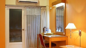 Quarto de hotel com uma escrivaninha de madeira, uma cadeira, um espelho, ar condicionado, luminária e cortina de chuveiro.