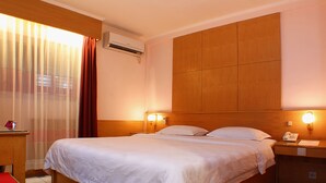 Quarto de hotel com uma cama grande, cabeceira de madeira, abajures e um tapete vermelho.