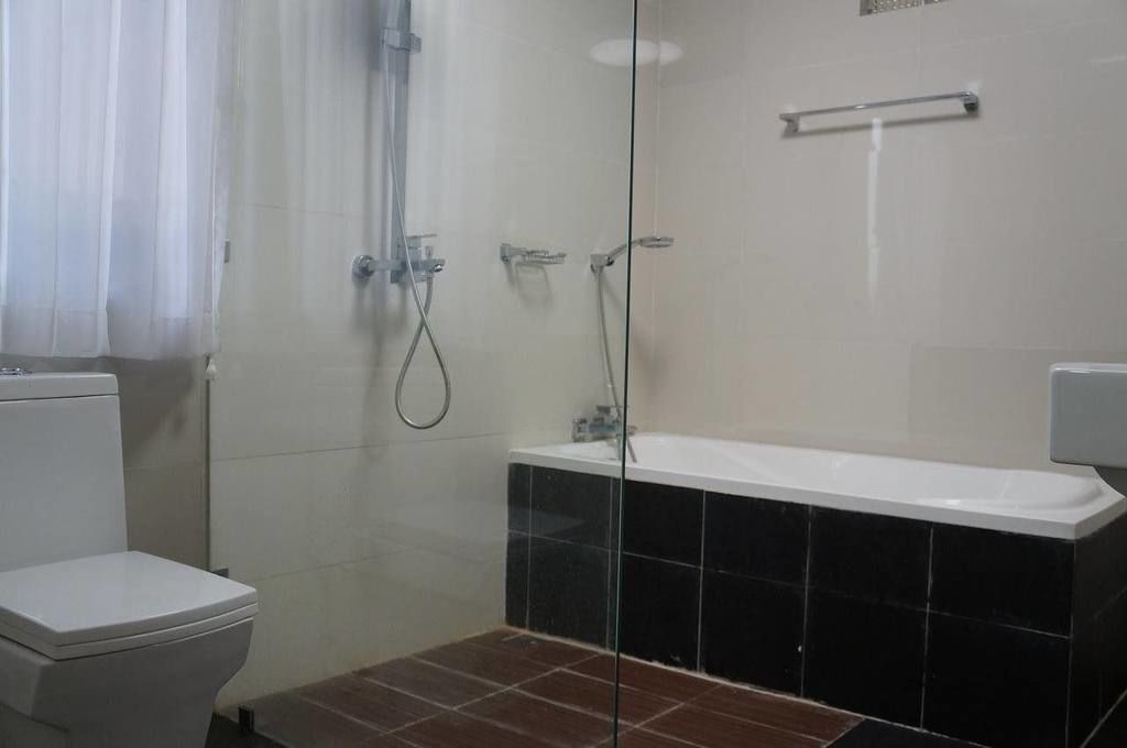 Casa de banho com sanita, zona de duche com divisória de vidro e banheira.