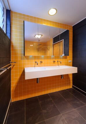 Casa de banho com uma pia branca, um espelho e azulejos laranja.