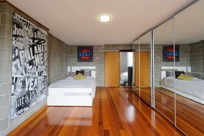 Quarto com um espelho grande, uma cama com cabeceira branca e uma parede com um cartaz grande.