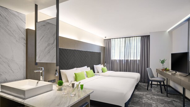 Quarto de hotel moderno com cama grande, escrivaninha, televisão e banheiro com pia de mármore.