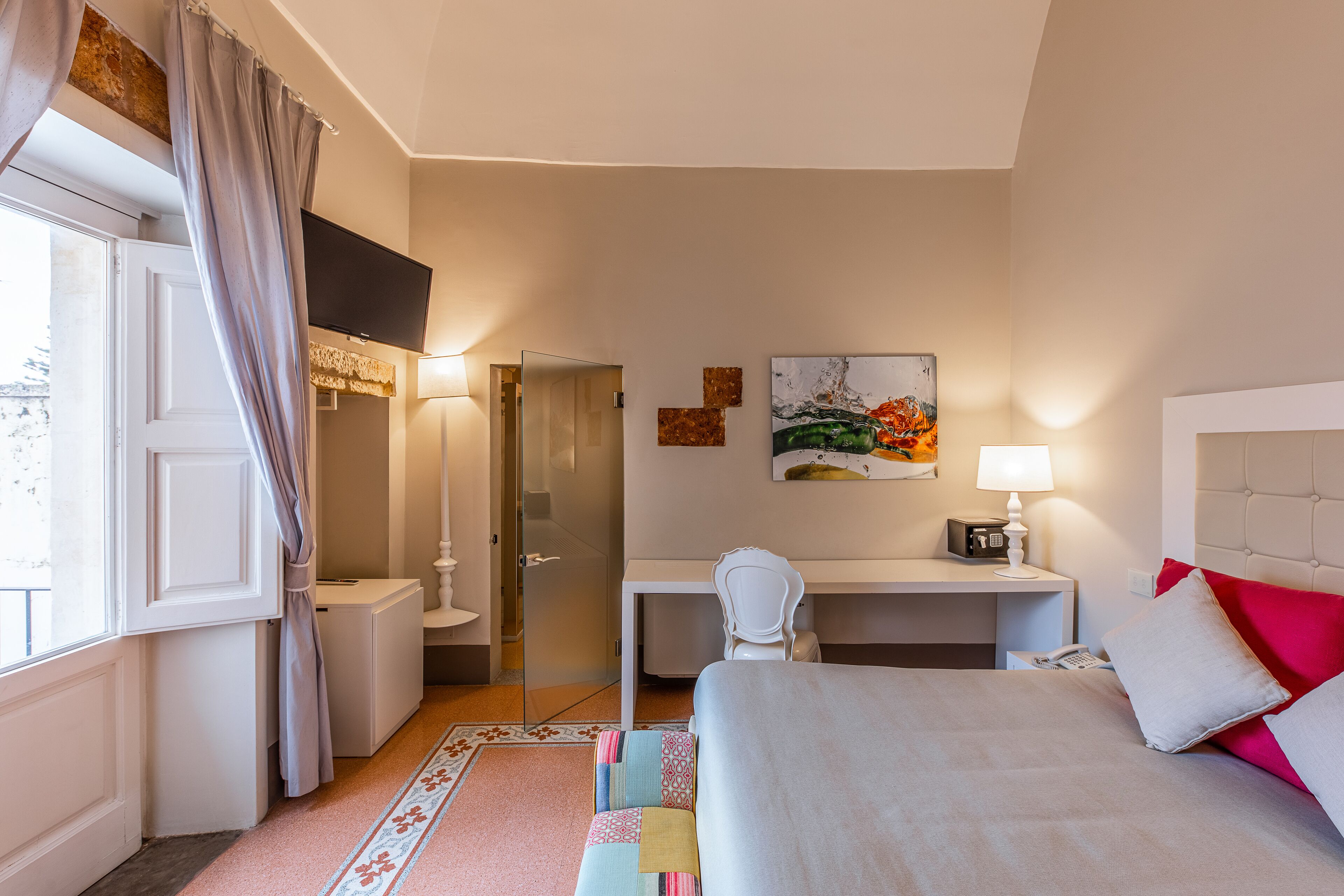 Quarto de hotel com cama, escrivaninha, cadeira e televisão.