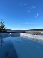 Uma banheira de hidromassagem com vista desobstruída para uma paisagem nevada e uma árvore ao primeiro plano.