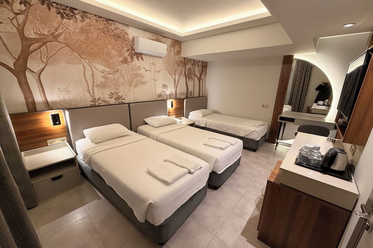 Quarto de hotel com duas camas, toucador com espelho, pia e parede com um mural de árvore.