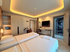 Quarto de hotel com duas camas, uma escrivaninha, chuveiro e televisão.