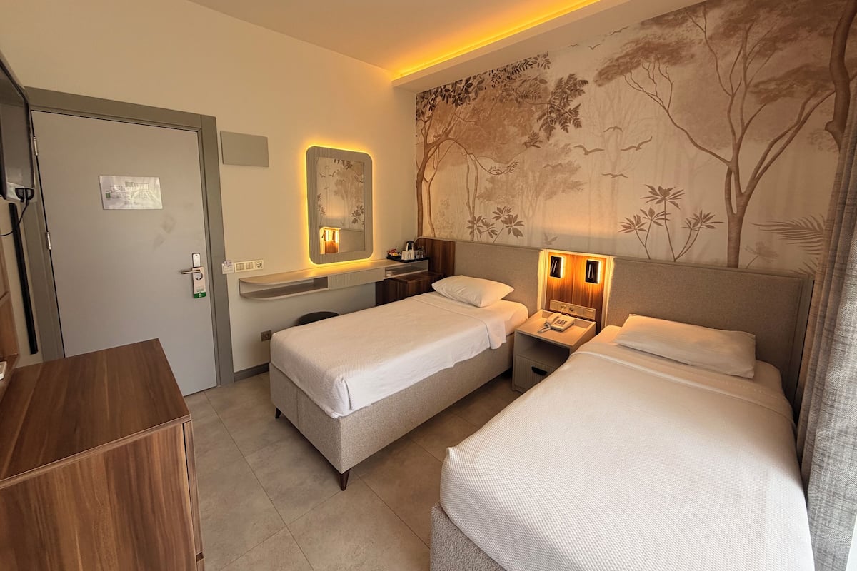 Quarto de hotel com duas camas, uma escrivaninha, um espelho e um mural na parede.