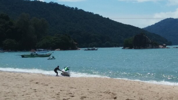 Uma praia com barcos e uma pessoa remando em um caiaque.