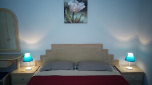 Quarto com cama, duas luminárias de cabeceira, mesa de cabeceira, cômoda e um quadro na parede.