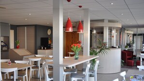 Restaurante moderno com mesas e cadeiras brancas, luminárias pendentes vermelhas e um vaso de flores vermelhas.