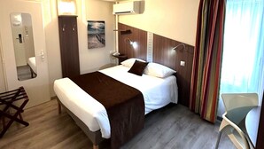 Quarto de hotel com cama, mesa de cabeceira, abajur e vista do exterior através das cortinas.