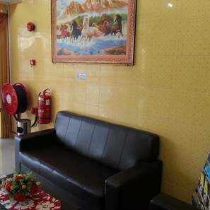 Um sofá de couro preto encostado em uma parede amarela, com um quadro de cavalos, um extintor de incêndio e um alarme de incêndio.