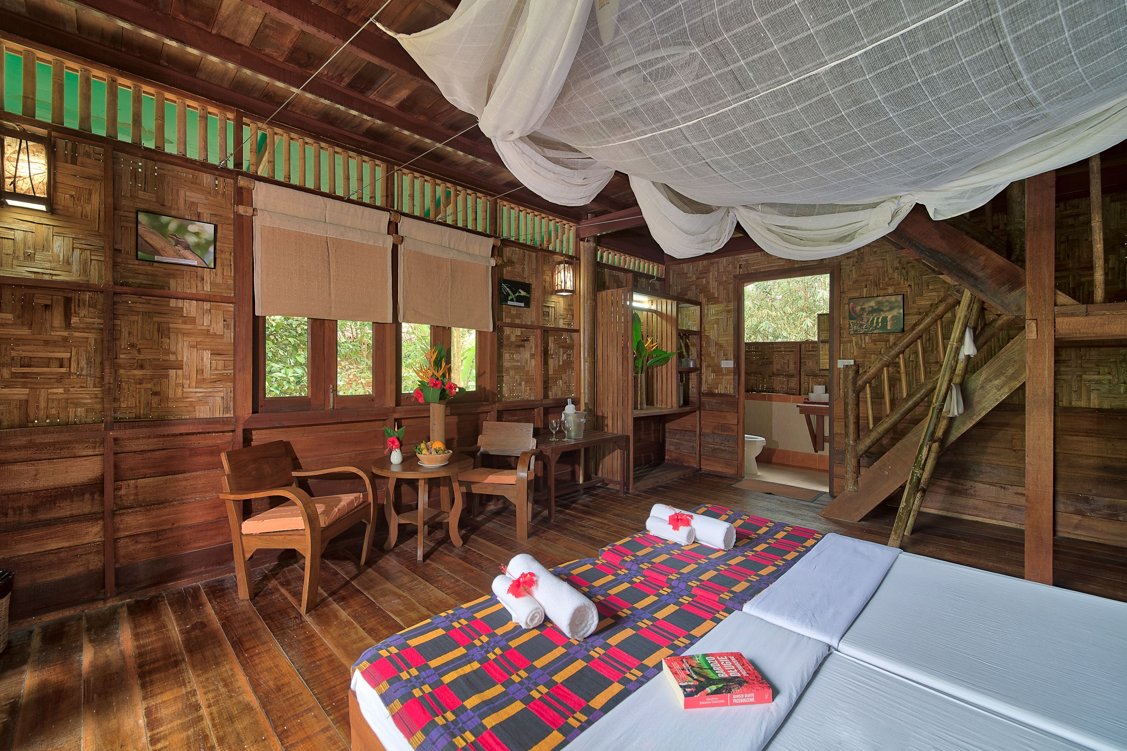 Uma cabana de madeira com uma cama, duas cadeiras, uma mesa pequena e uma escada.