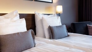 Quarto de hotel com cama bem arrumada, mesa de cabeceira com abajur e quadros na parede.
