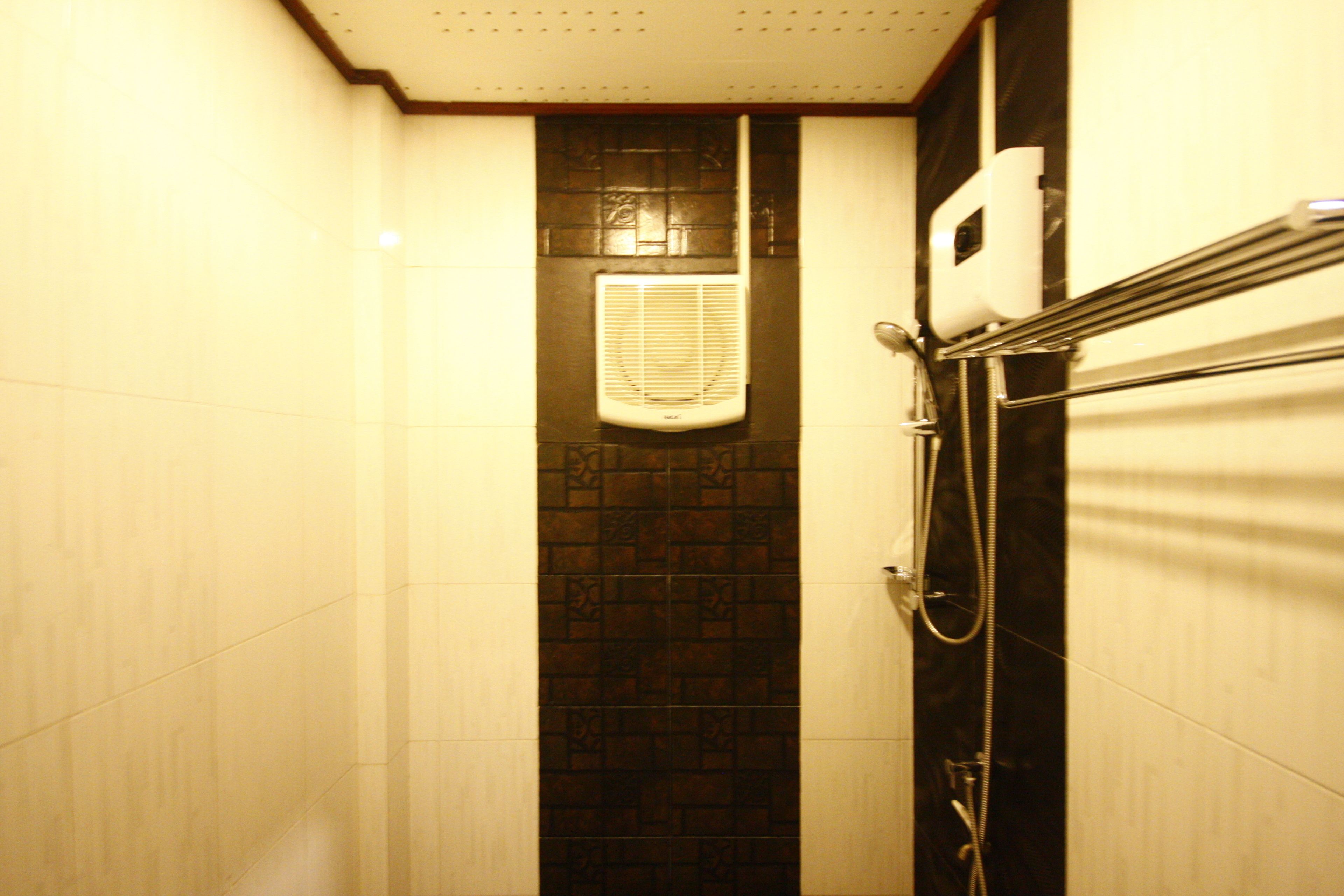 Casa de banho estreita com chuveiro, porta-toalhas e ventilação.