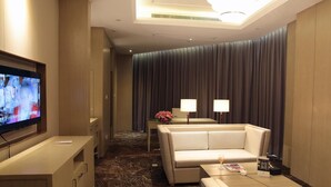 Quarto de hotel com televisão, sofá, mesa de centro, escrivaninha e luminária.
