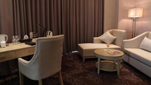 Quarto de hotel com uma escrivaninha, duas poltronas, um sofá, uma mesinha redonda e um abajur.